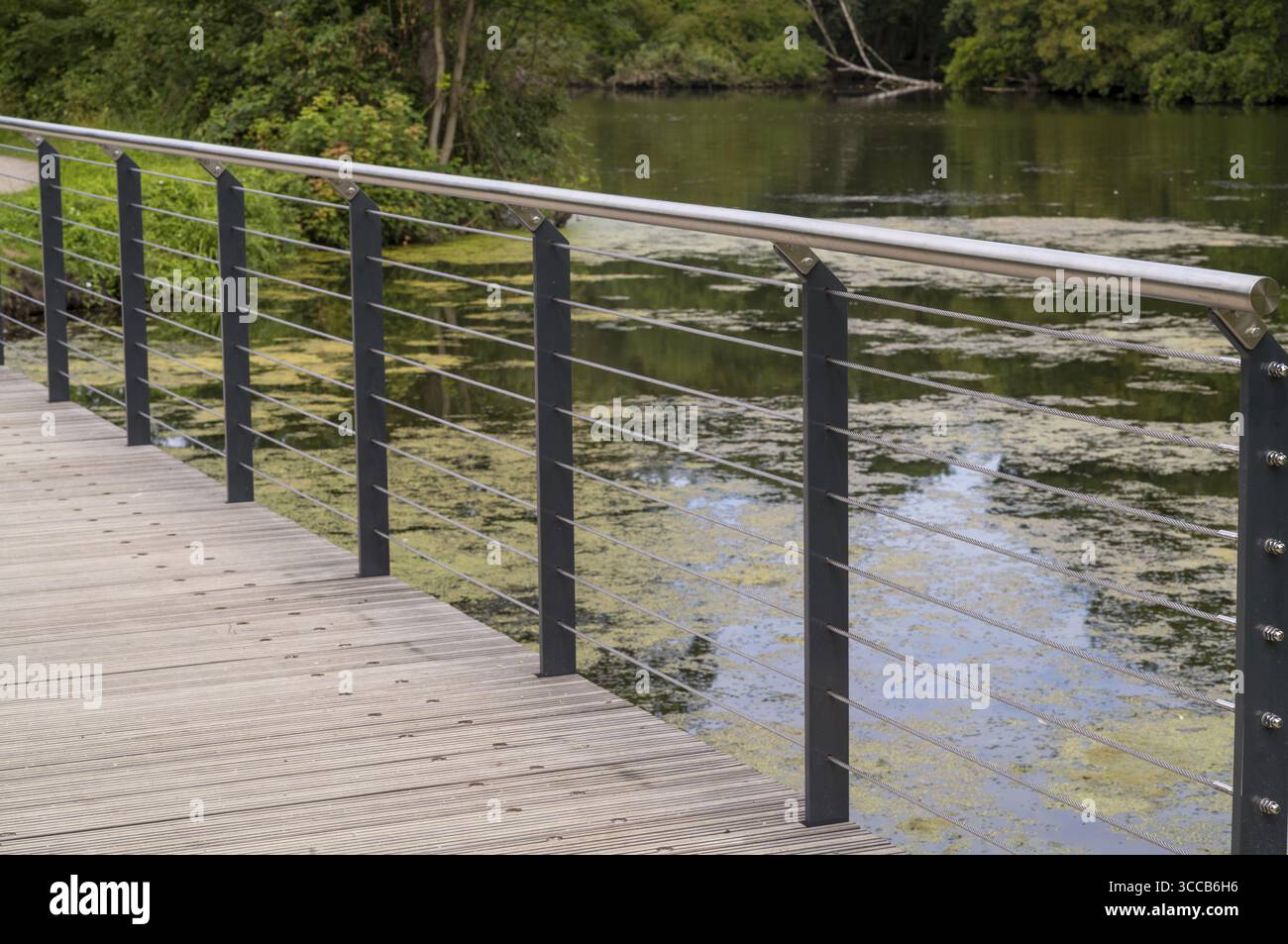 Wooden walkway with modern stainless steel cable railing and a pond in ...