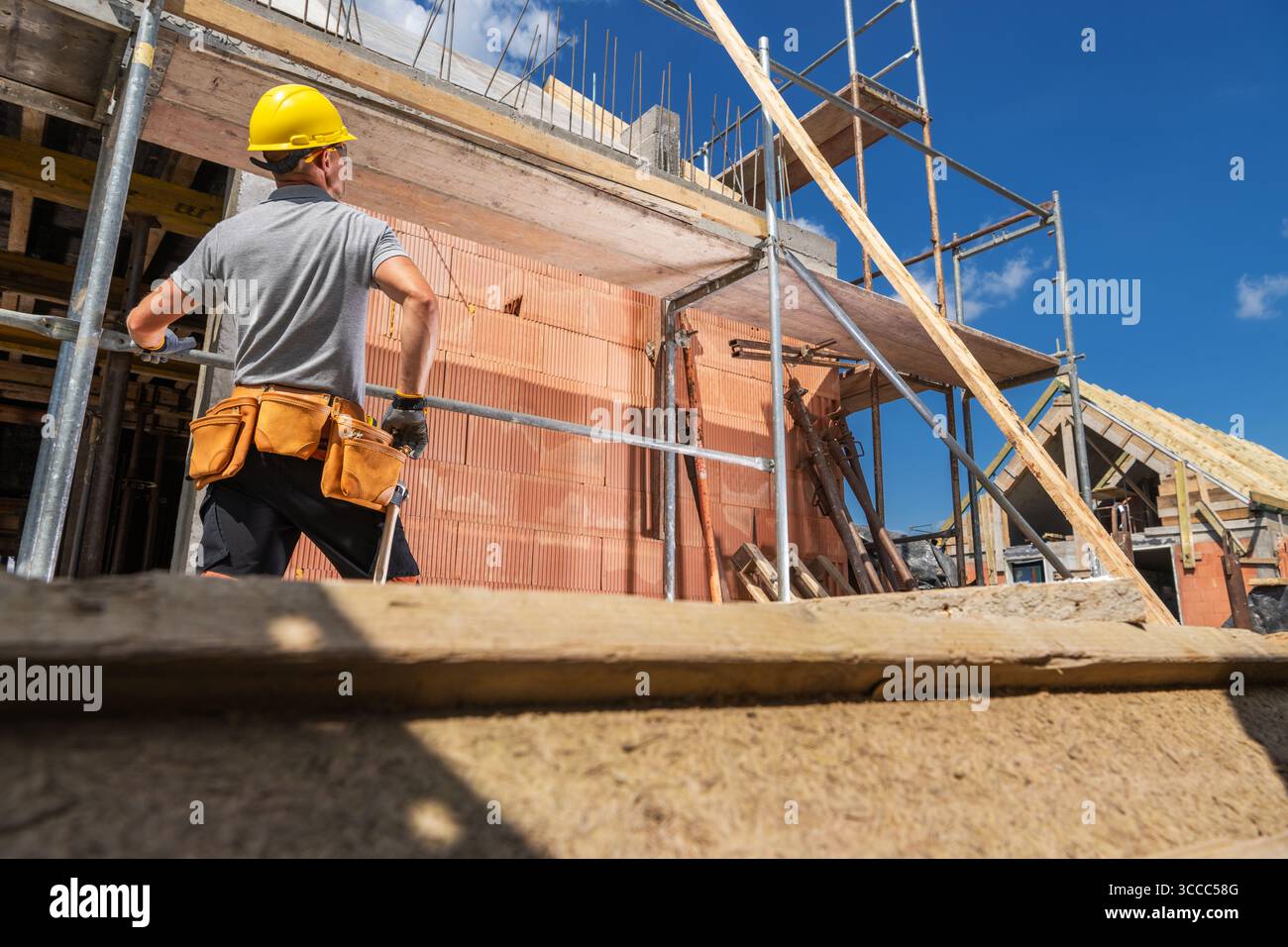 A construction worker wearing a yellow hard hat watches the progress of ...