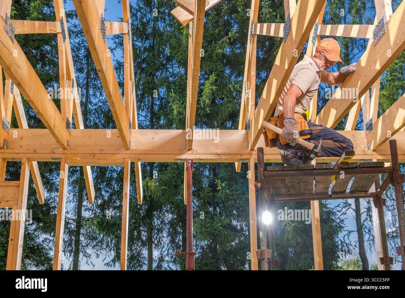 A carpenter is focused on constructing wooden framework while perched ...