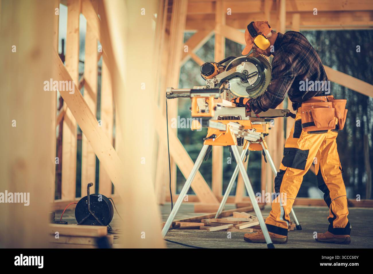 A focused carpenter operates a miter saw inside a wooden frame ...