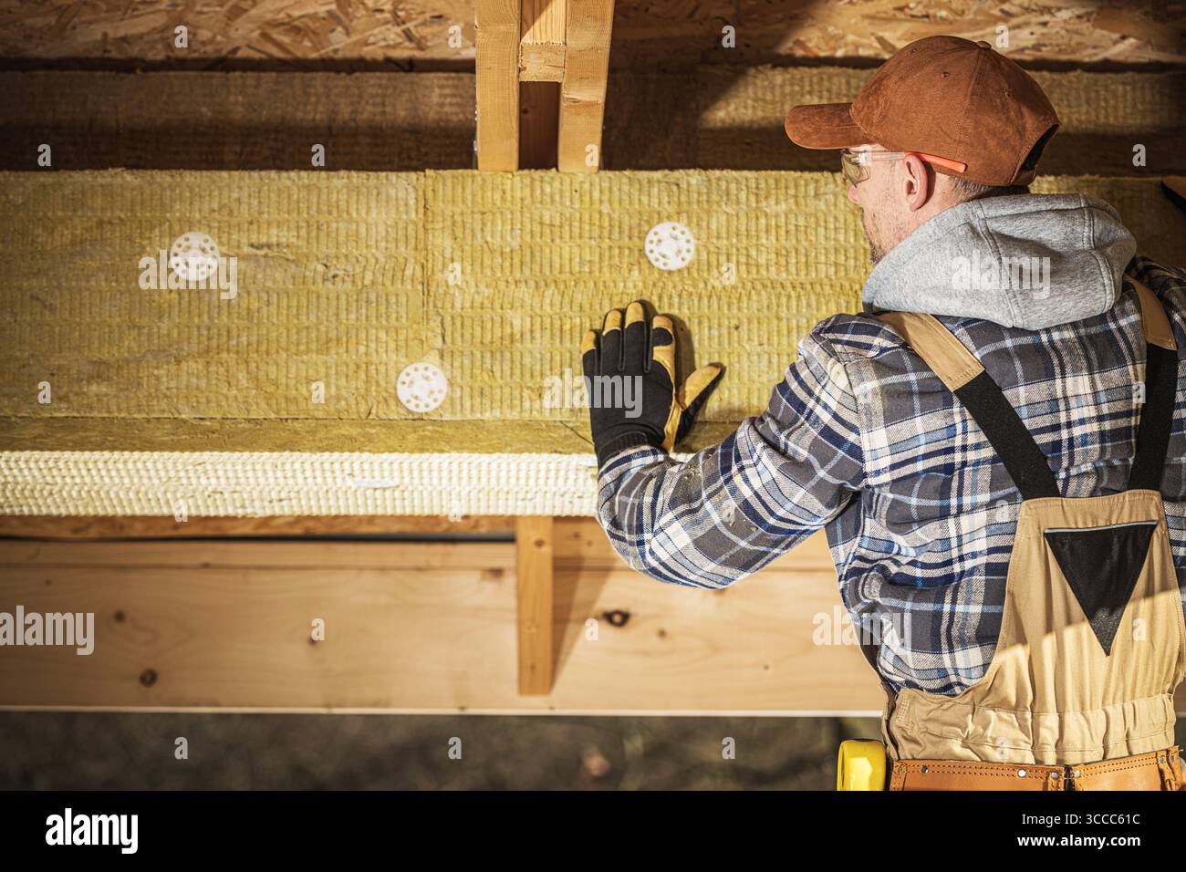 A construction worker carefully installs insulation on wooden beams in ...