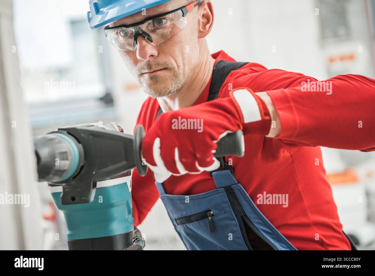 A construction worker wearing safety gear operates a power tool at a ...