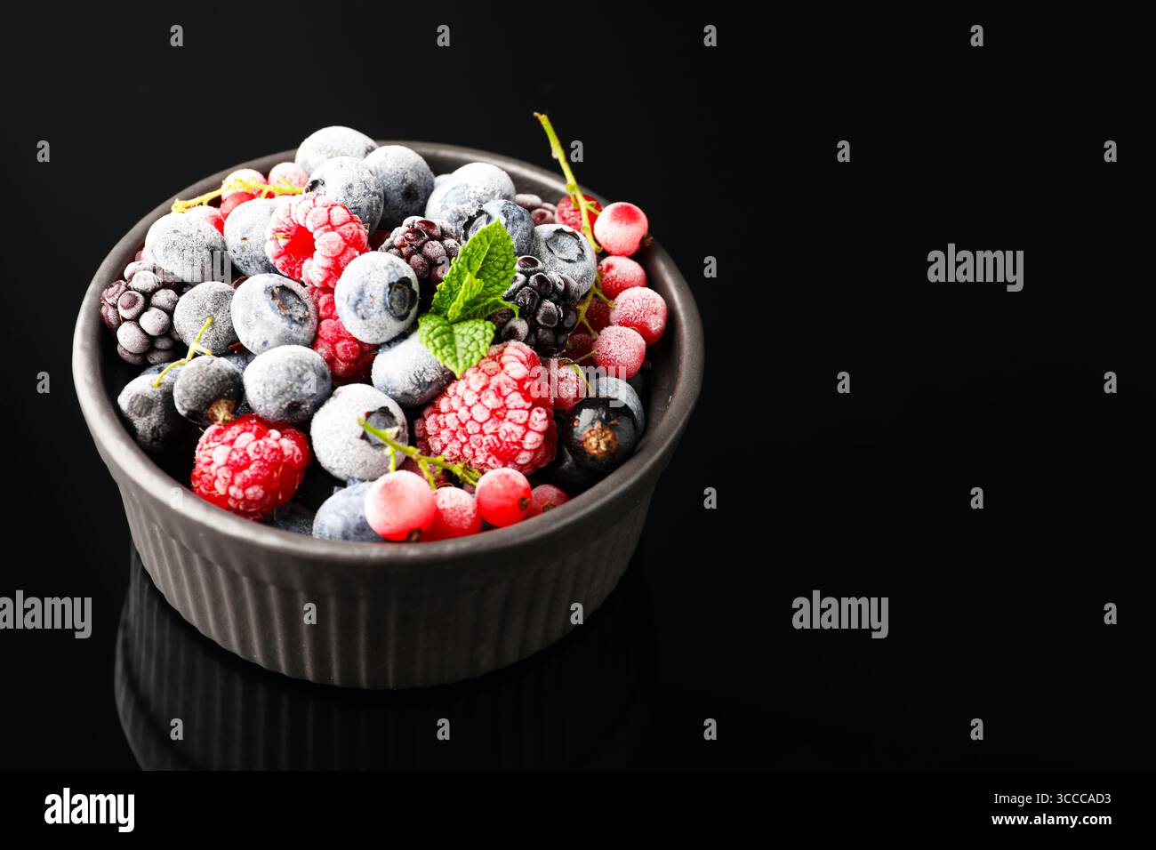 Many different frozen berries and mint in bowl on black table, closeup ...