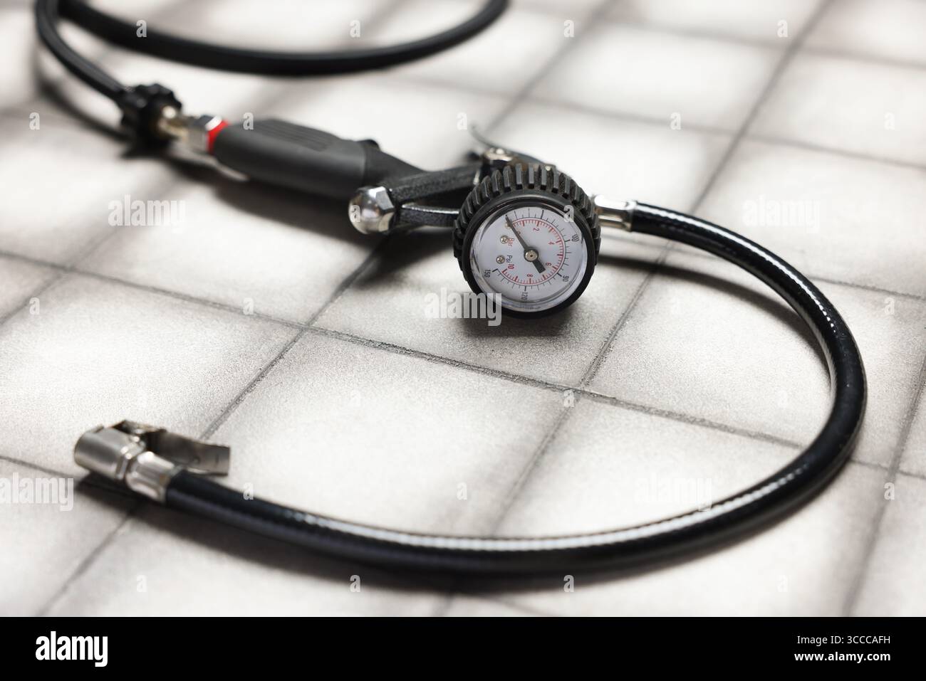One tire inflation gun with gauge on light tiled background, closeup ...