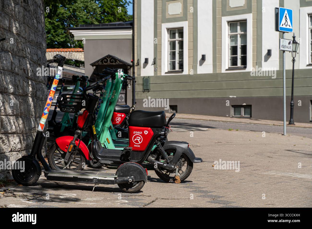 Shared electric scooter and moped parked by a stone wall near a ...