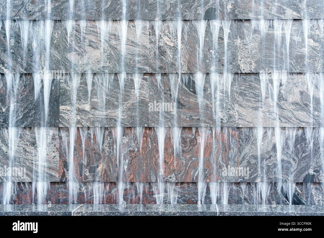 Water cascades down textured marble tiles in a layered wall fountain at ...