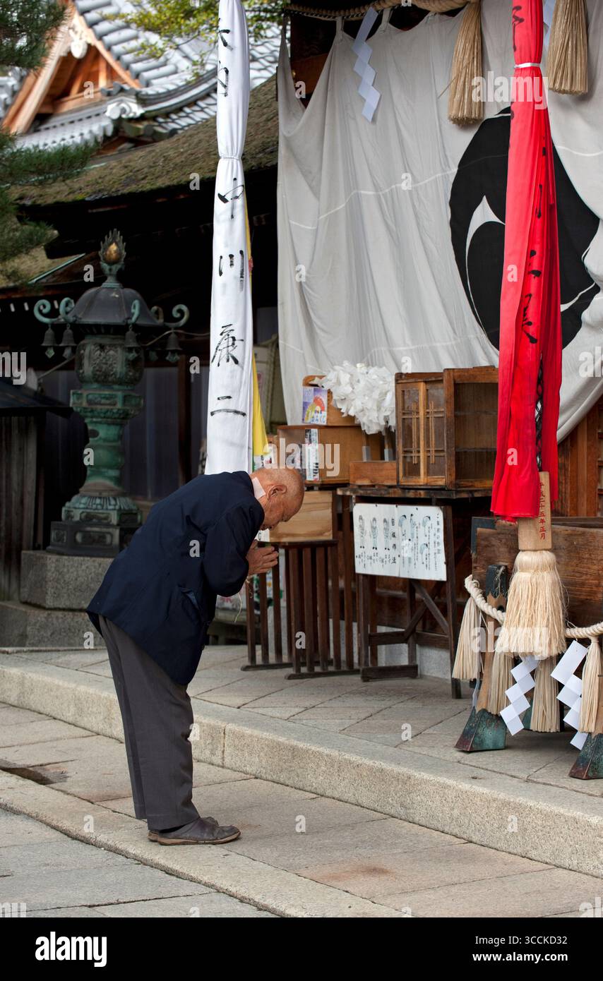 Japanese senior citizen bowing while praying to the deity in front of ...