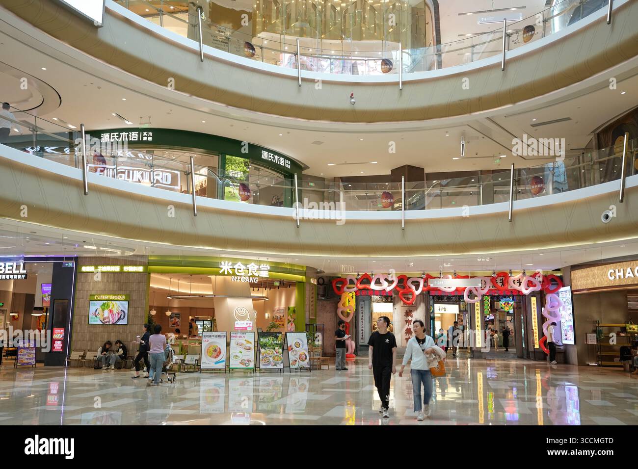 Inside a shopping mall, escalators hum under high ceilings as shoppers ...