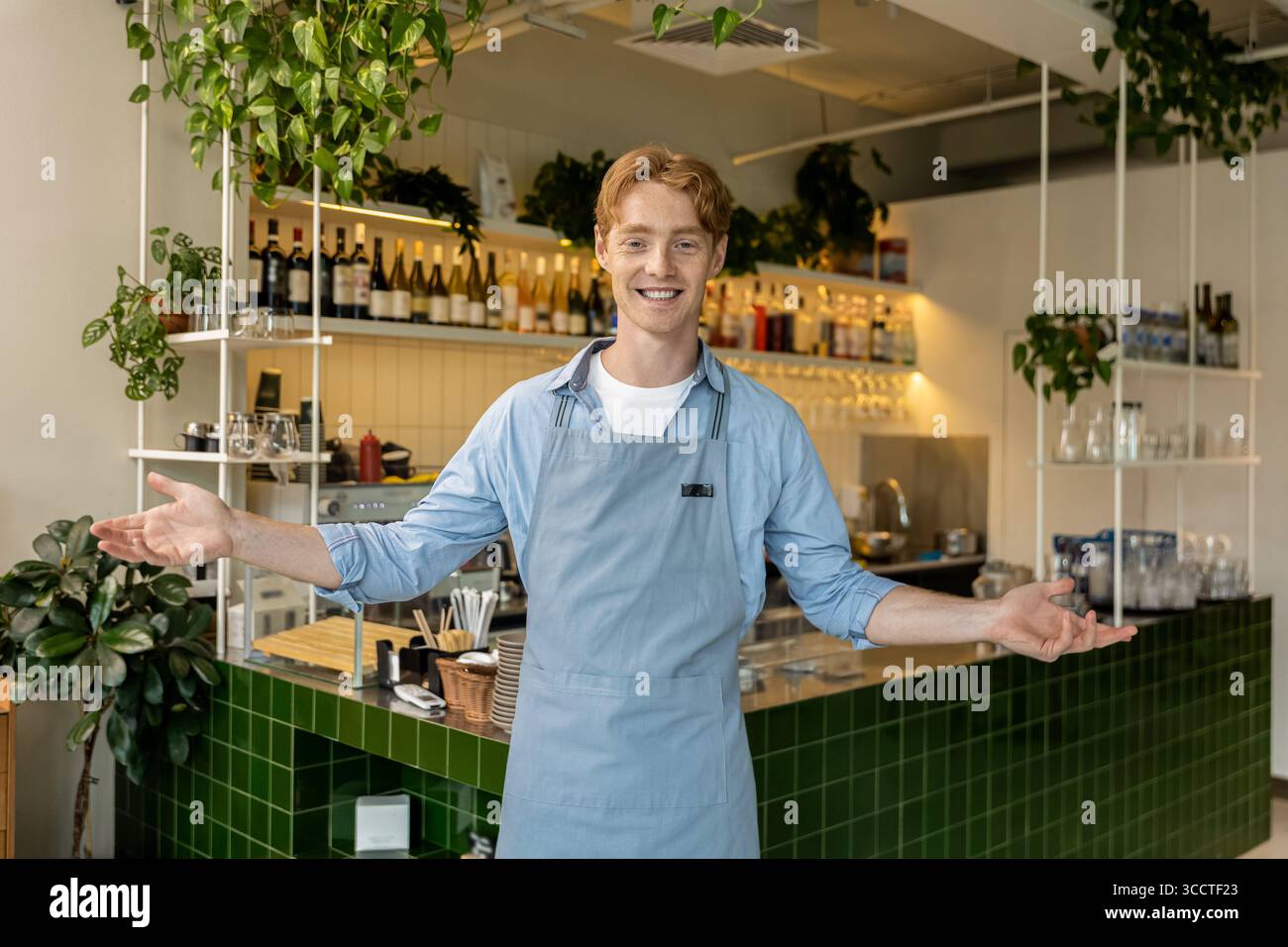 Cheerful male barista with apron smiling and welcoming guests with open ...