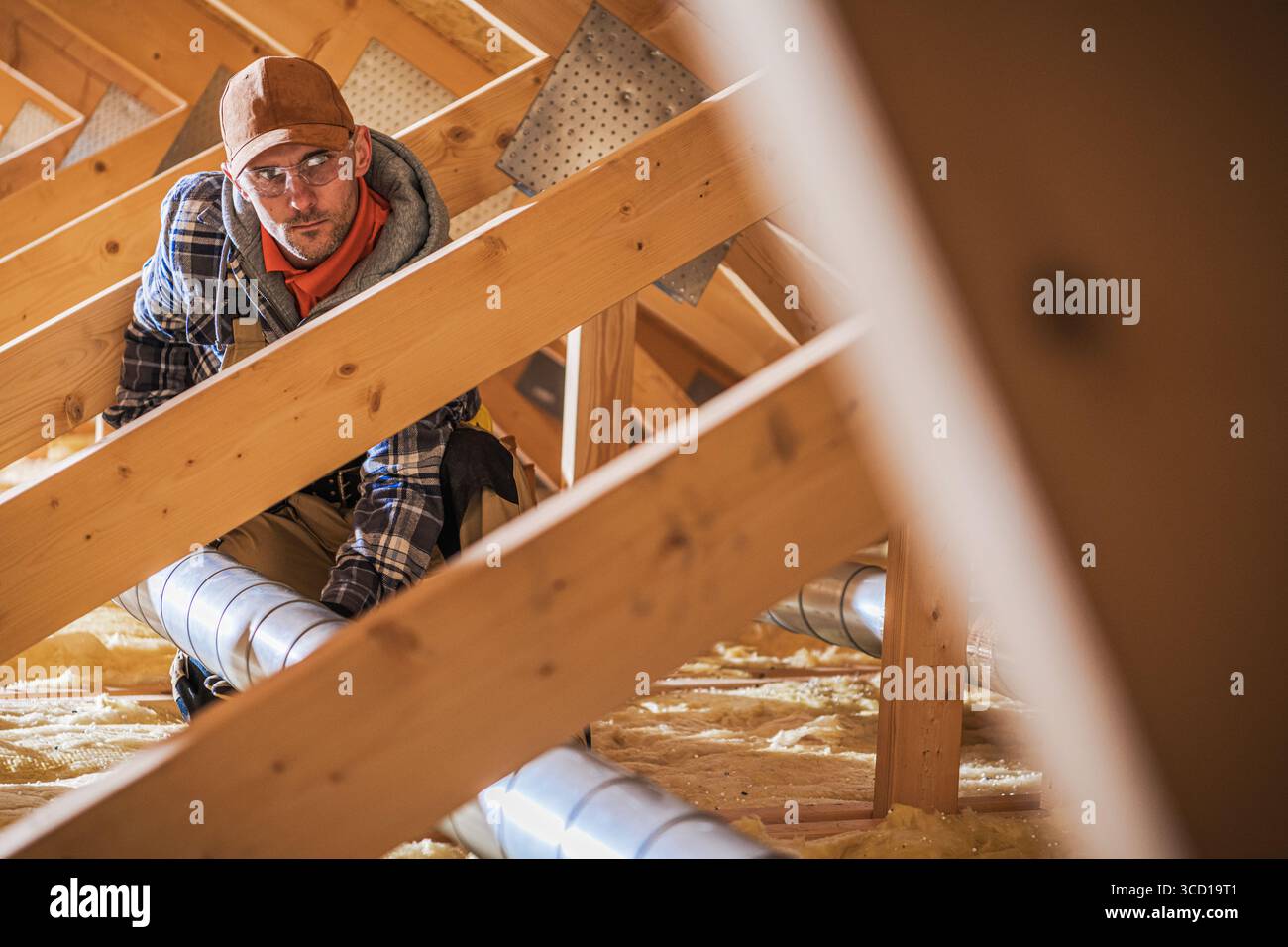 A HVAC worker examines insulation and ventilation pipes in an attic ...