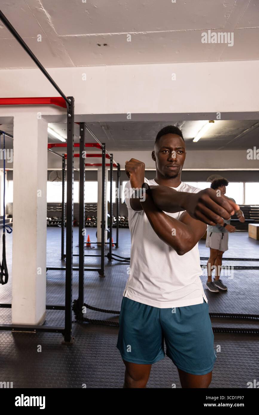 Diverse male friends stretching arms in gym with squat rack, battle ...