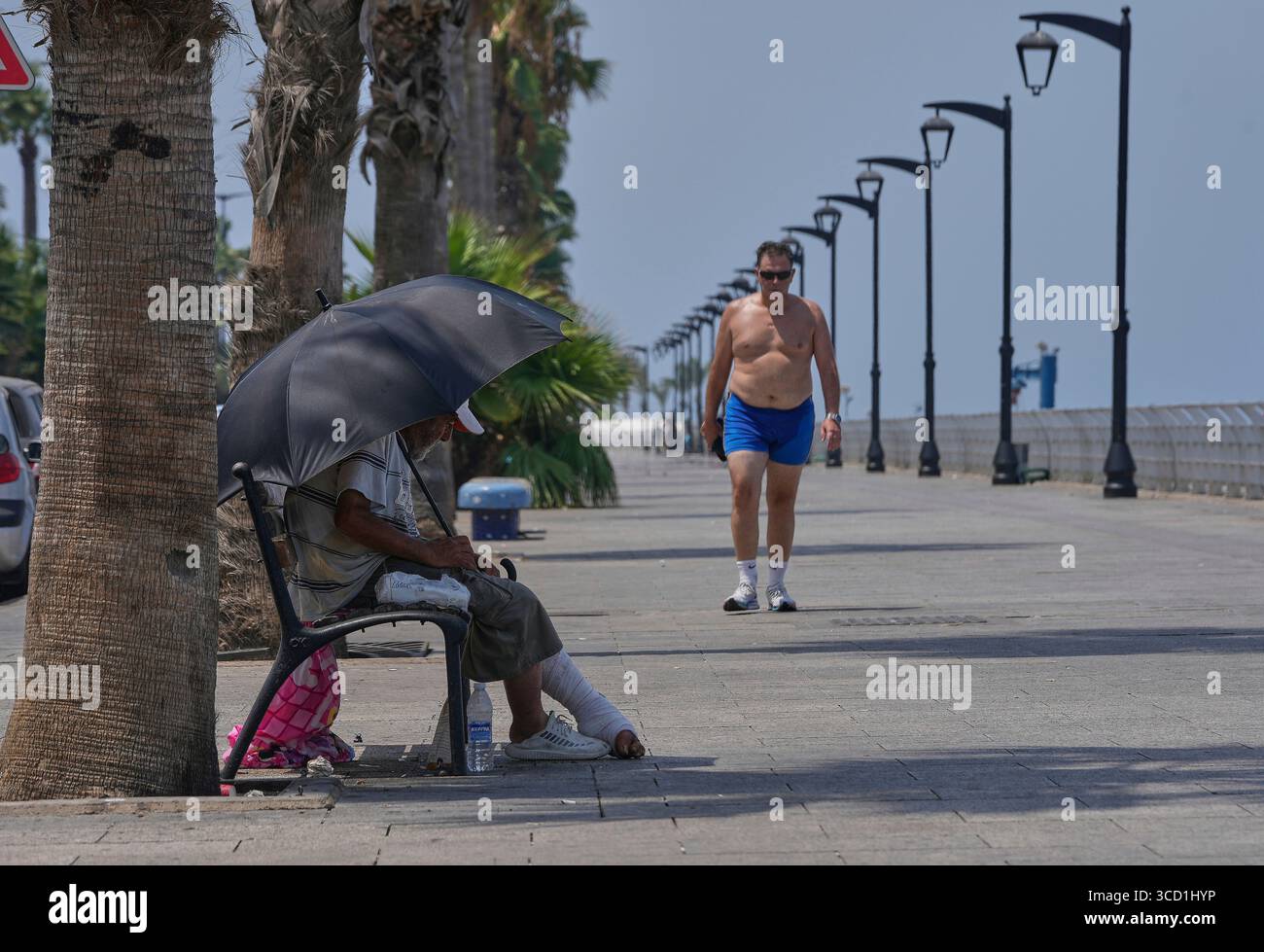 A homeless man uses an umbrella to shield himself from the sun and the ...