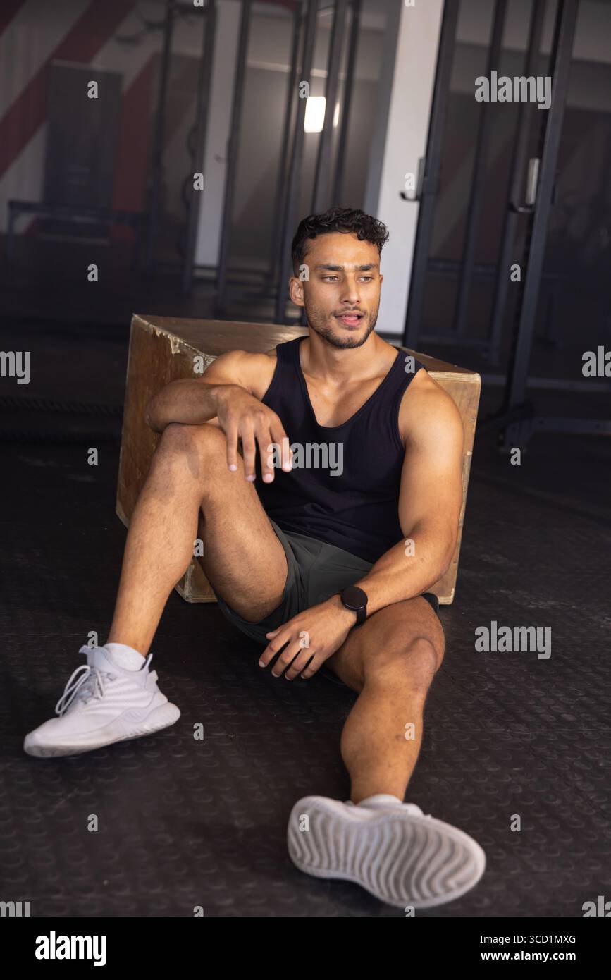 Asian man sitting on gym floor leaning against plyometric box wearing ...