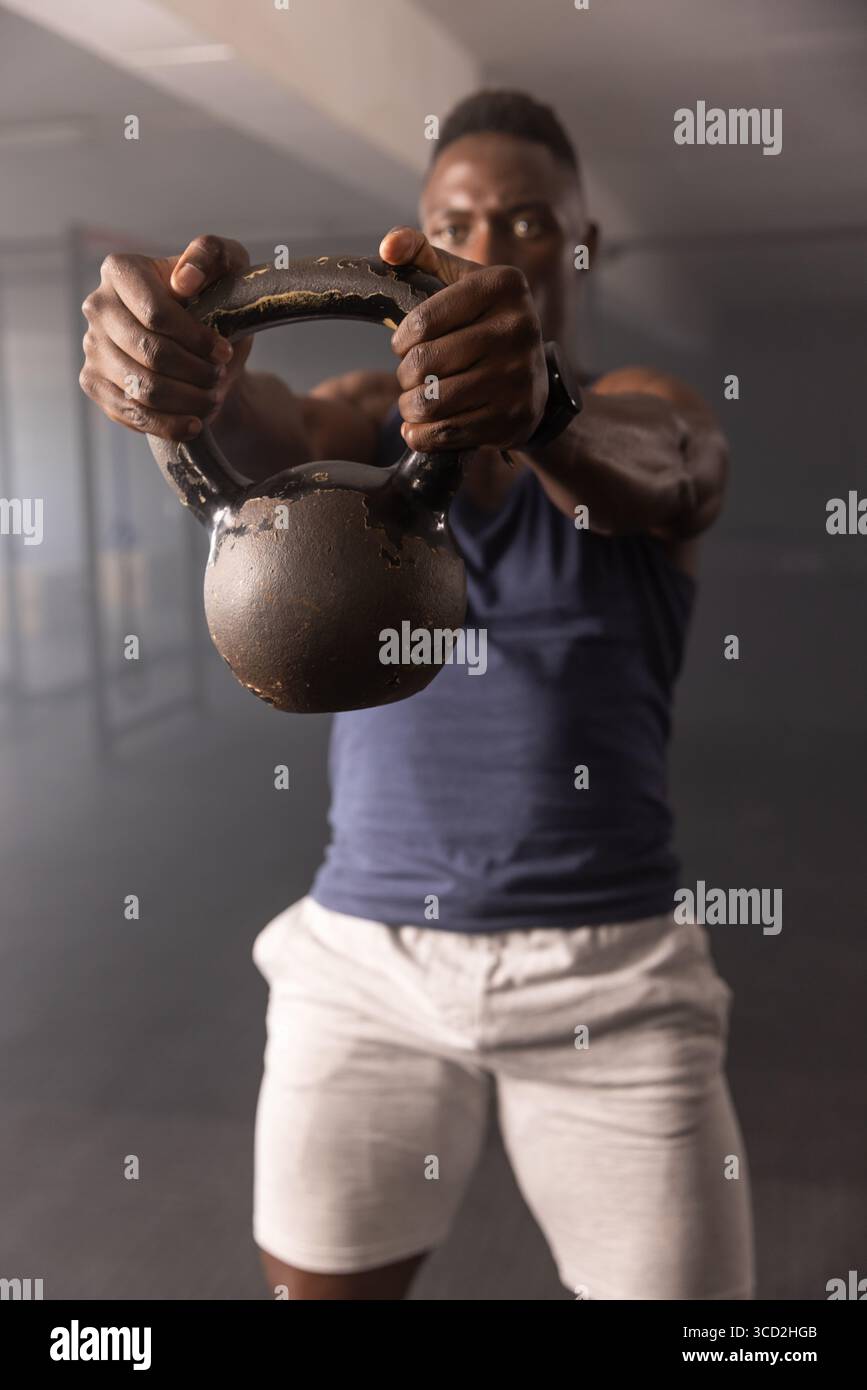 Fit man holding kettlebell at chest height in gym area with rubber ...