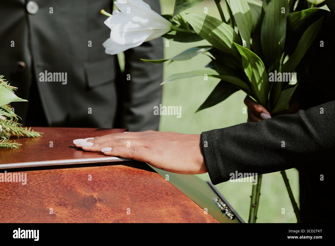 Black woman placing hand on wooden casket while holding lily bouquet ...
