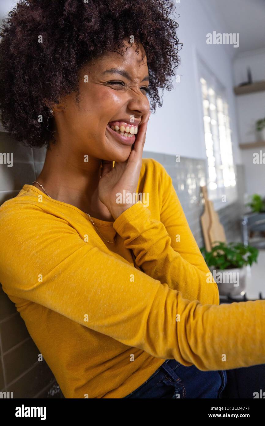 African American woman laughing touching cheek in kitchen, backsplash ...