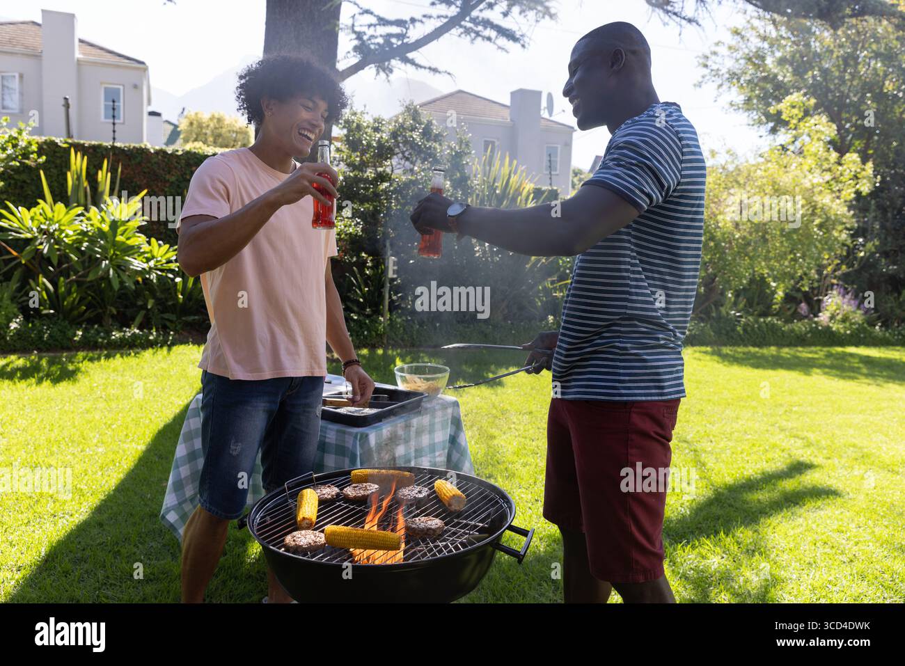 Diverse male friends raising red drinks while grilling corn and burgers ...
