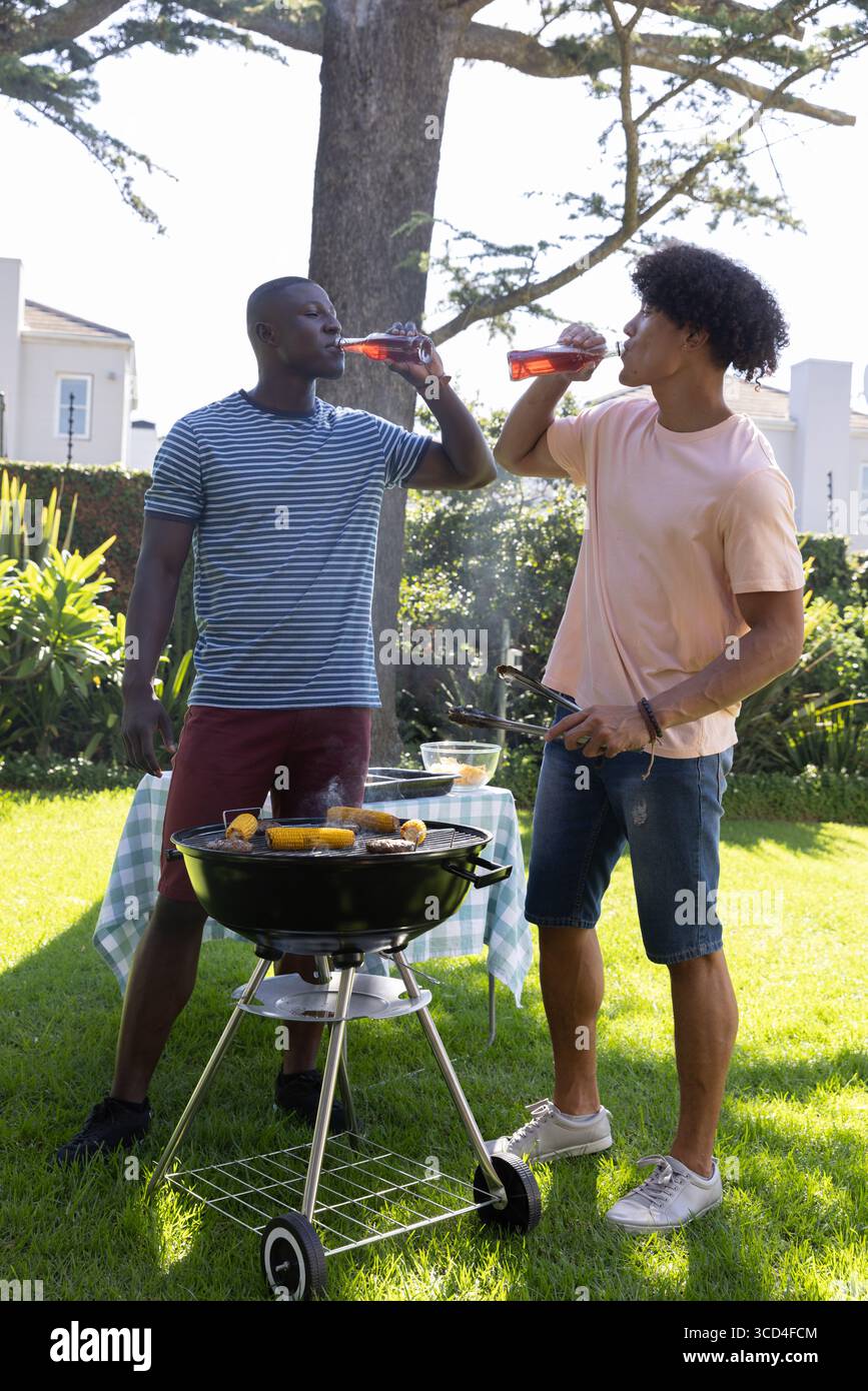 Diverse male friends grilling corn on charcoal grill in backyard while ...
