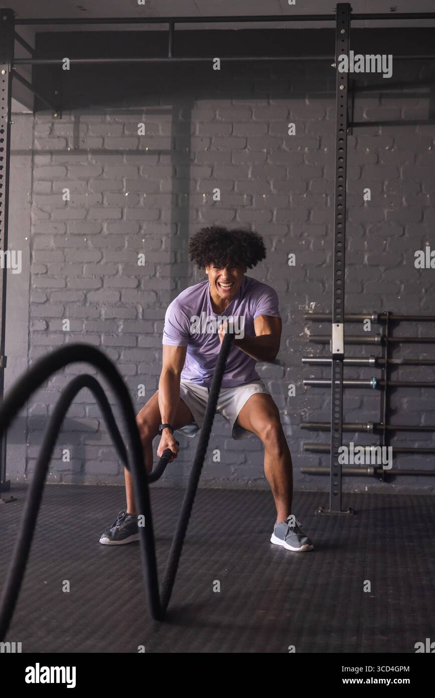 Athlete swinging heavy battle ropes in weight area by brick wall, with ...