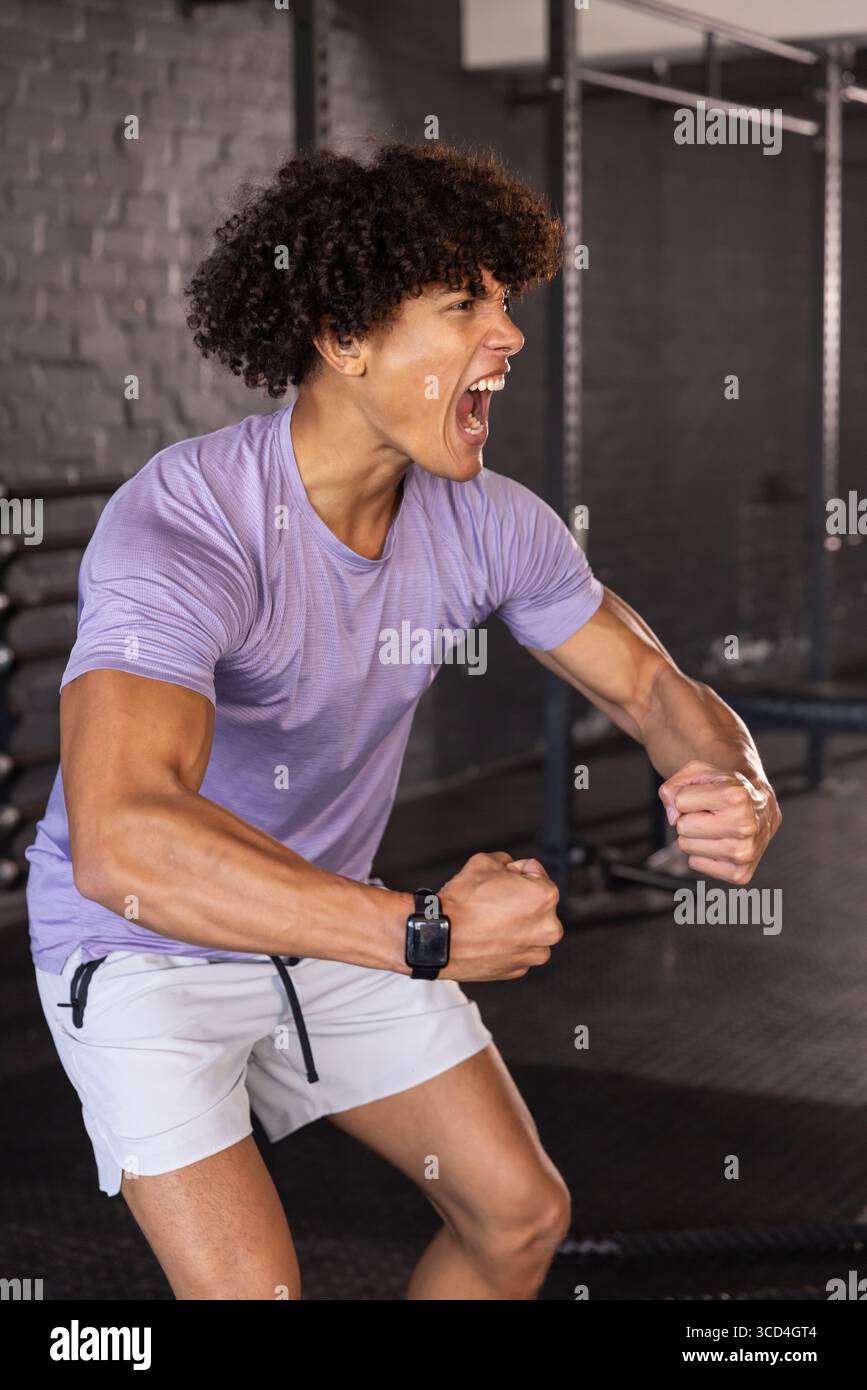 Muscular athlete flexing biceps and shouting in brick-walled gym with ...