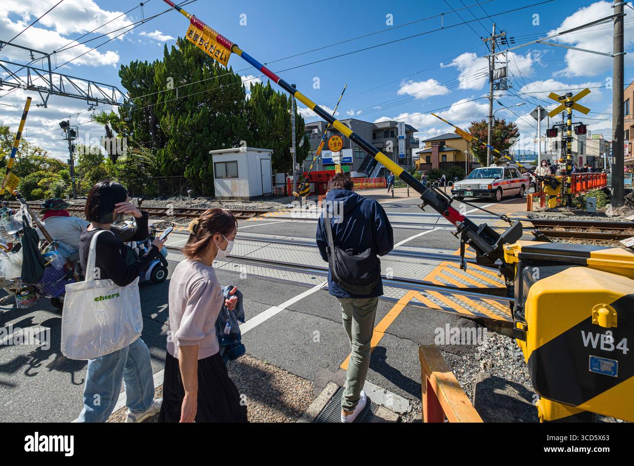 People walking under rising barricade at level crossing, Fukakusa Inari ...
