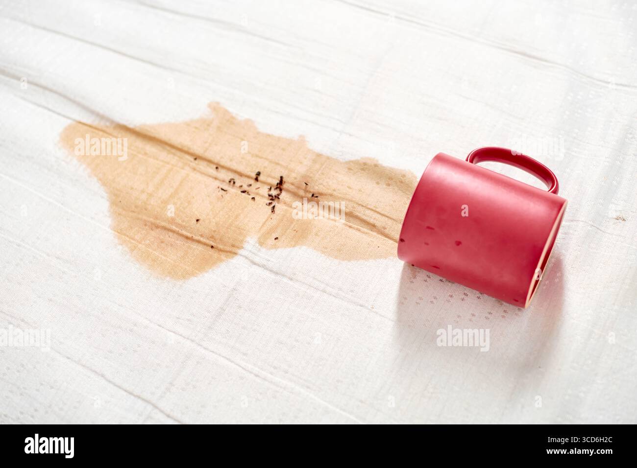 Red mug lies on side, spilling coffee onto white fabric. Light coffee ...