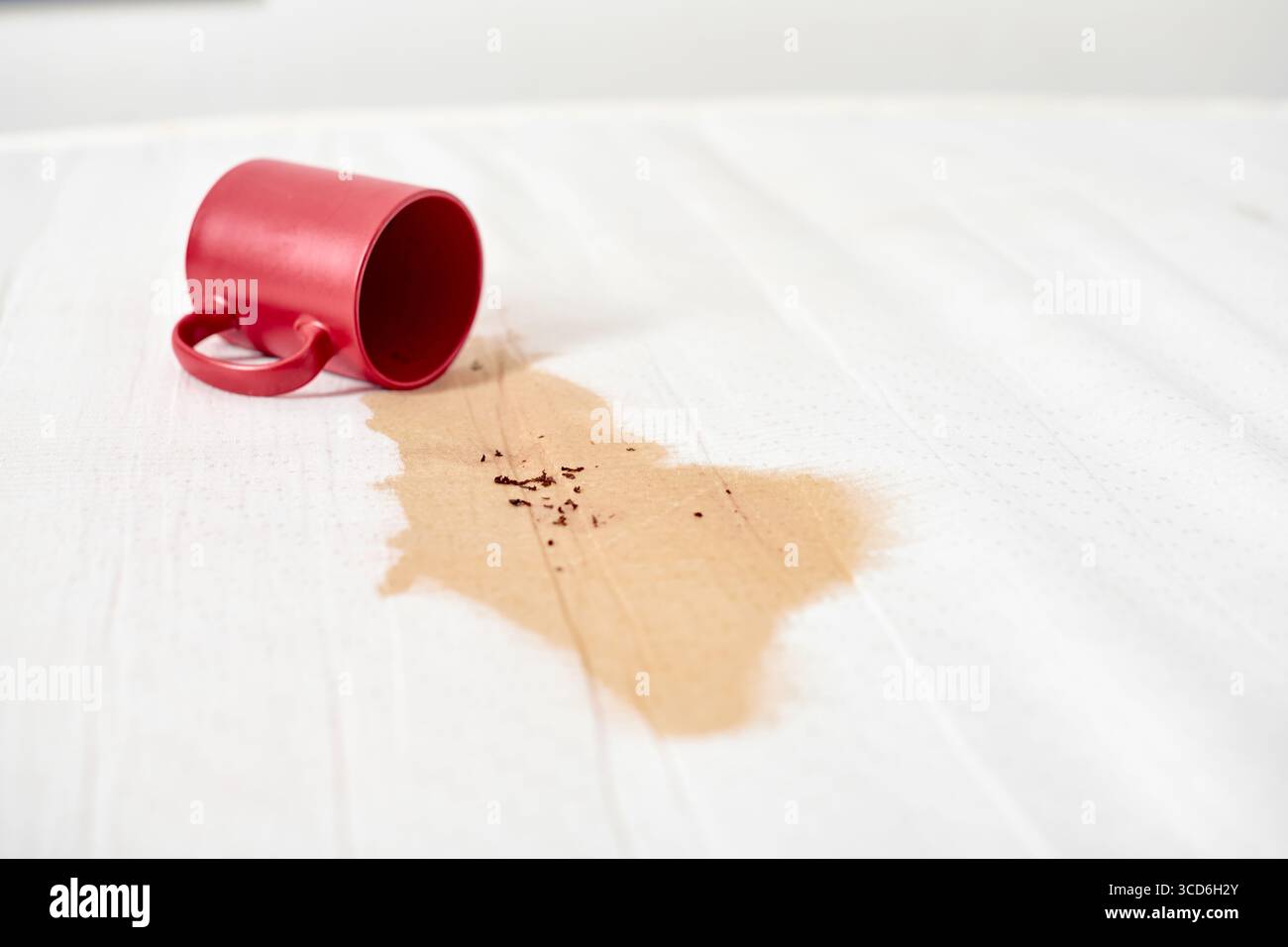 Red mug lies tipped over, spilling coffee onto white textured surface ...
