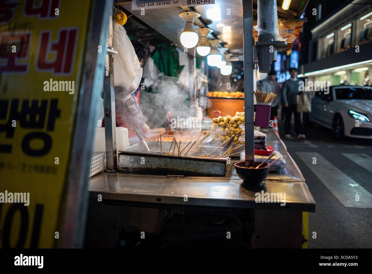 A bustling Korean street food stall at night, featuring skewers and ...