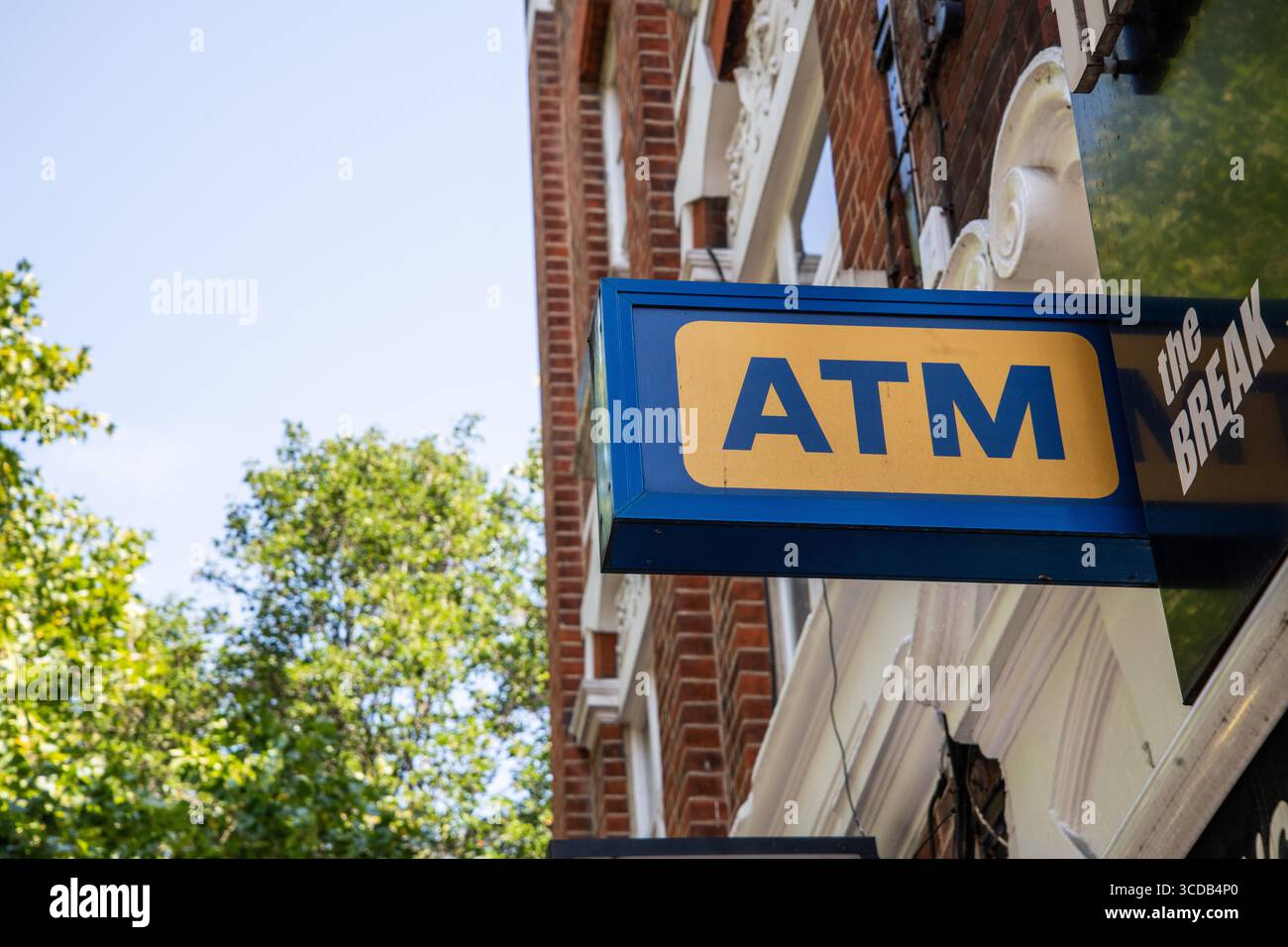 Blue and yellow “ATM” sign mounted outside a shop, indicating cash ...