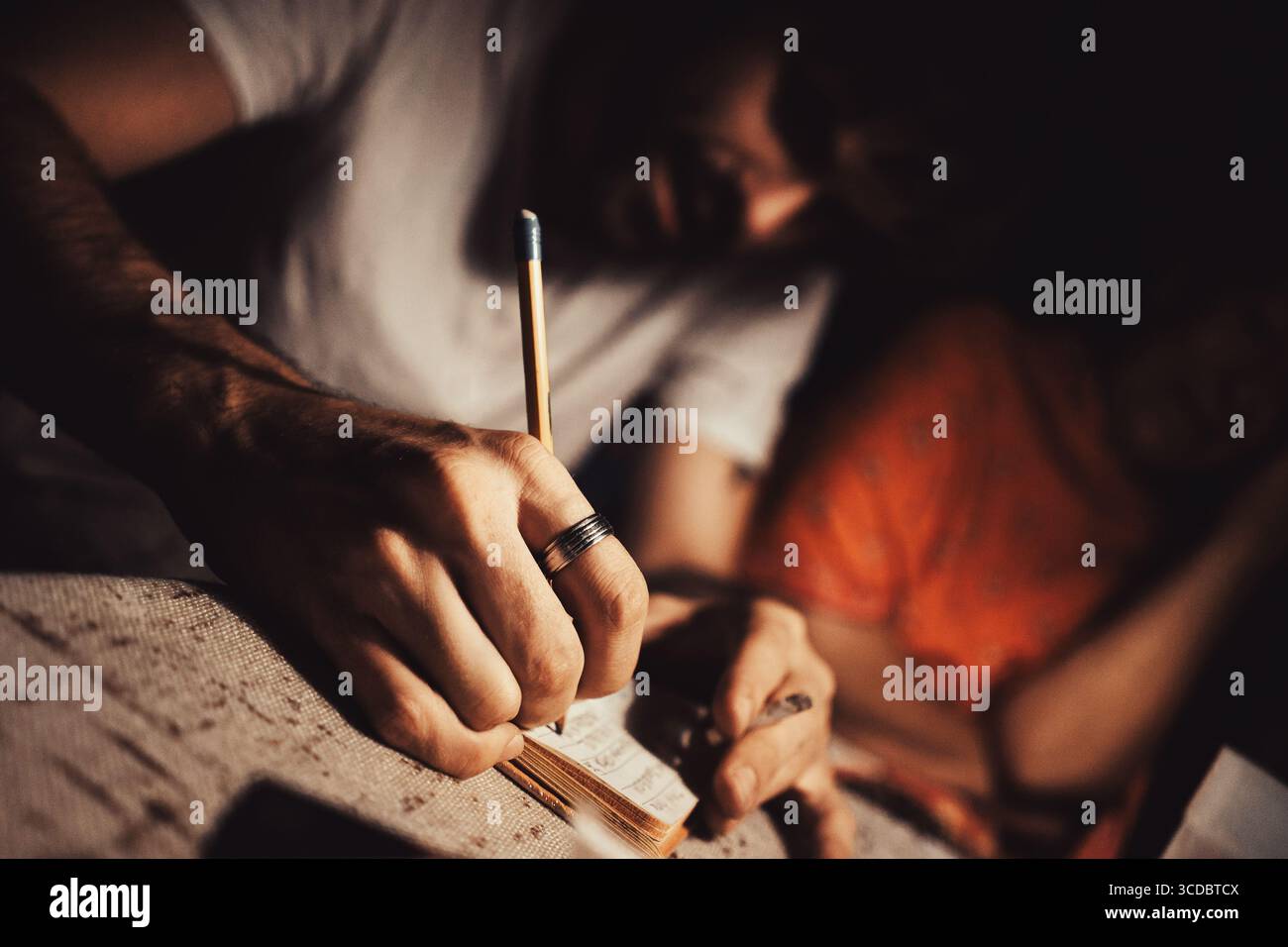 Hands of young man with ring in focus, taking notes or jotting down ...