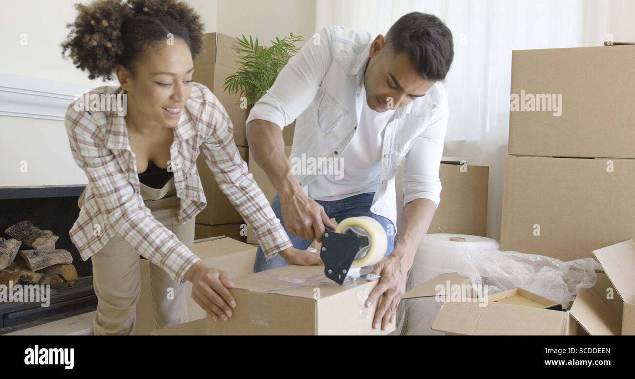 Young couple taping boxes as they pack up their home to move to a new ...