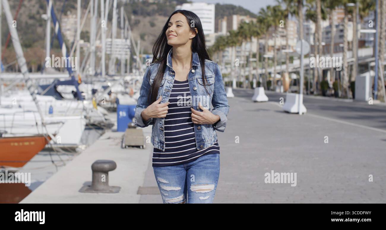 Trendy jaunty young woman enjoying a stroll along a waterfront ...