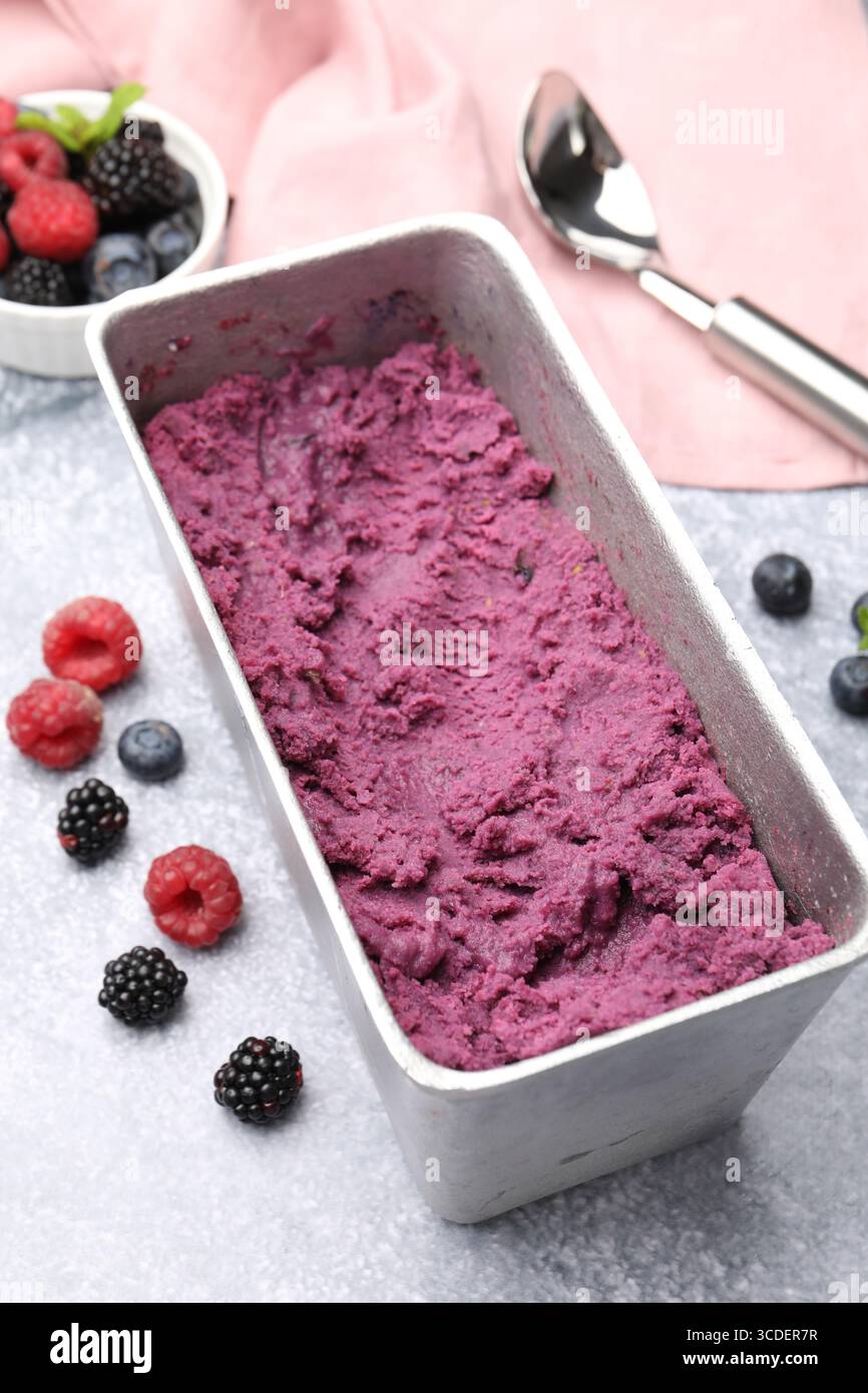 Delicious sorbet in metal container, fresh berries and spoon on grey ...
