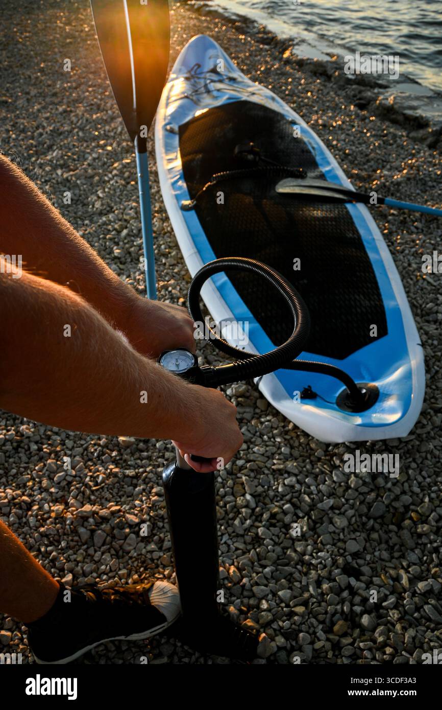 Sportsman inflating sup board with hand pump on pebble beach at sunset ...