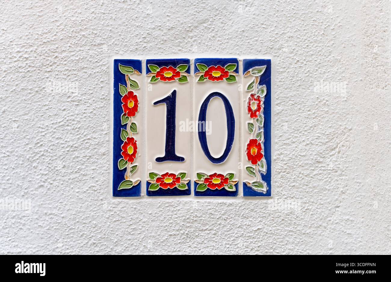 Decorative house number 10 tile with floral border on white stucco wall ...