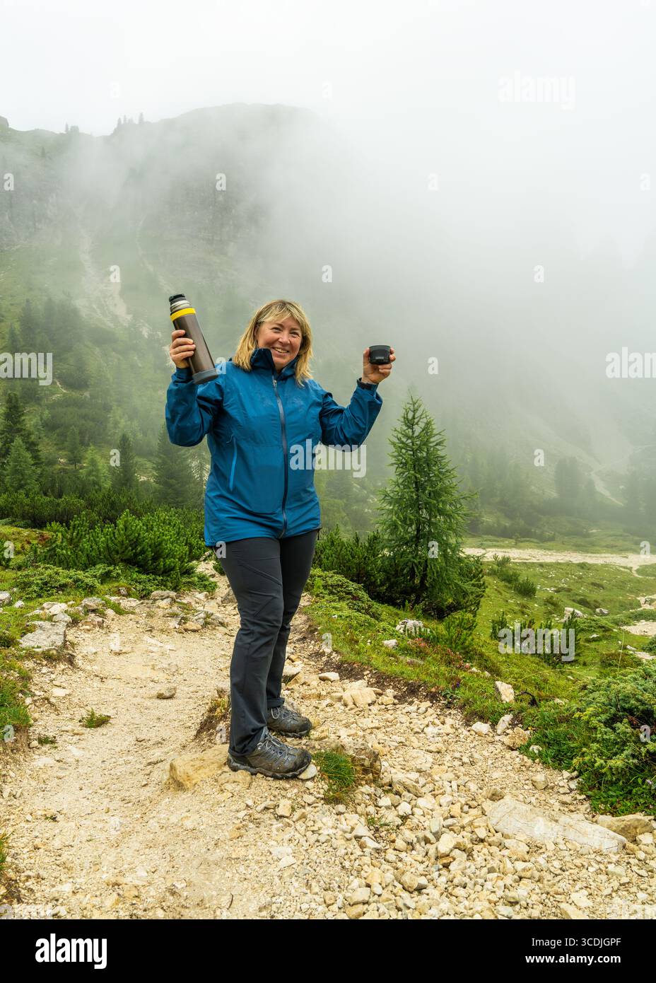 Vertical photo of middle aged woman in rain jacket hiking in Dolomites ...