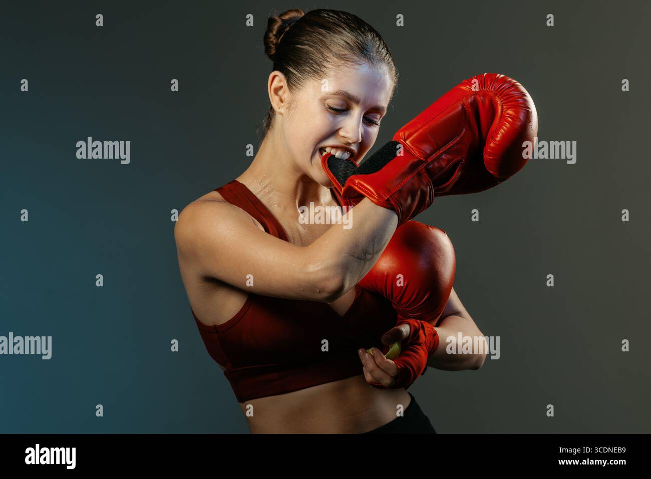 Young athlete in red gloves biting a glove after training on a dark ...