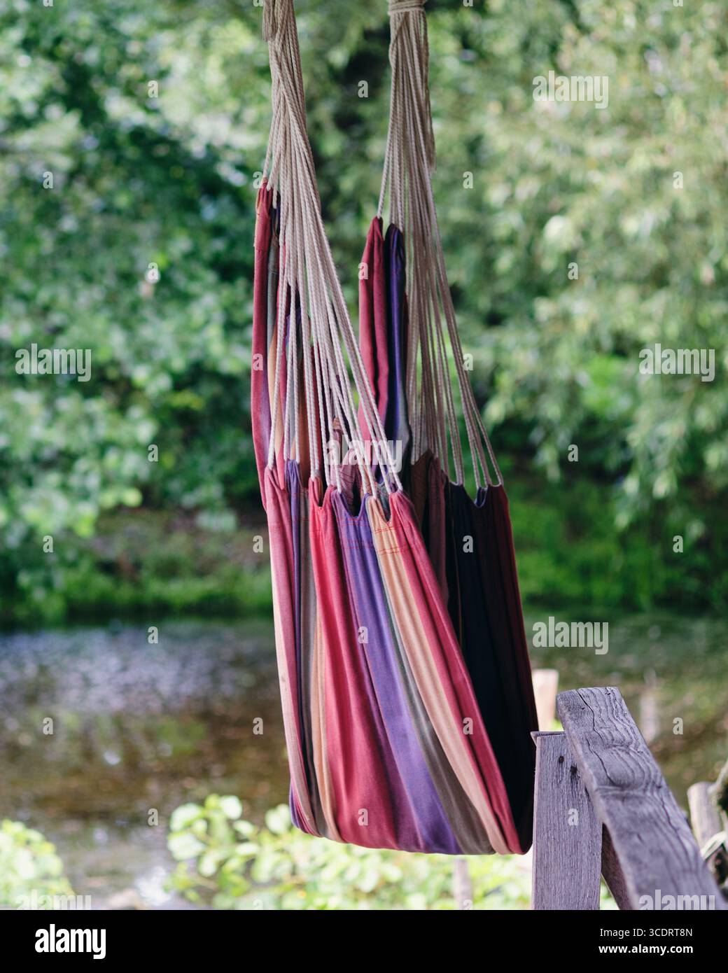 A colorful hammock hangs relaxed between two wooden posts near a calm ...