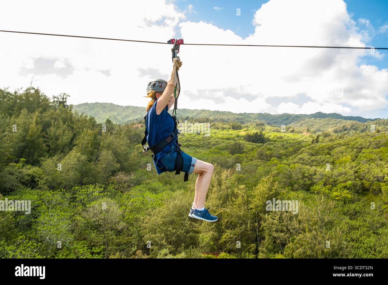 Woman in climbing harness suspended below pully speeding down aerial ...
