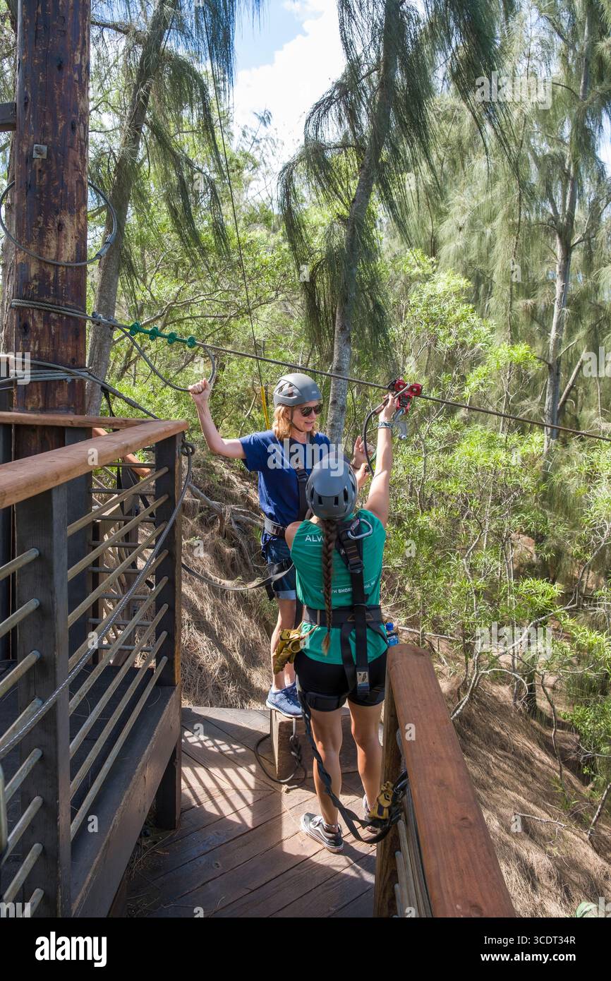 Guide checking safety equipment of female client during a zip-line tour ...