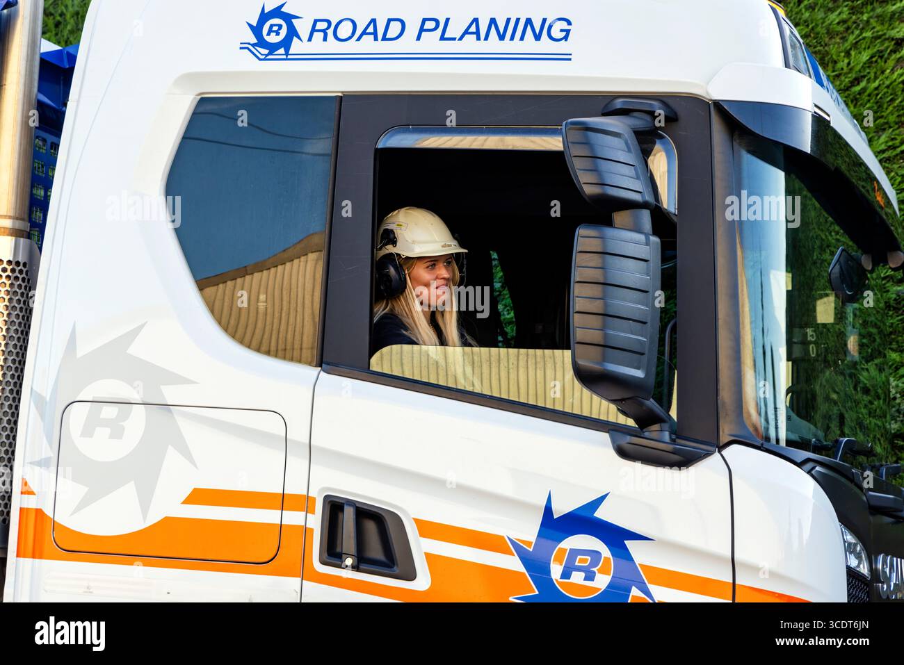 Female driver wearing hard hat, road resurfacing construction works ...