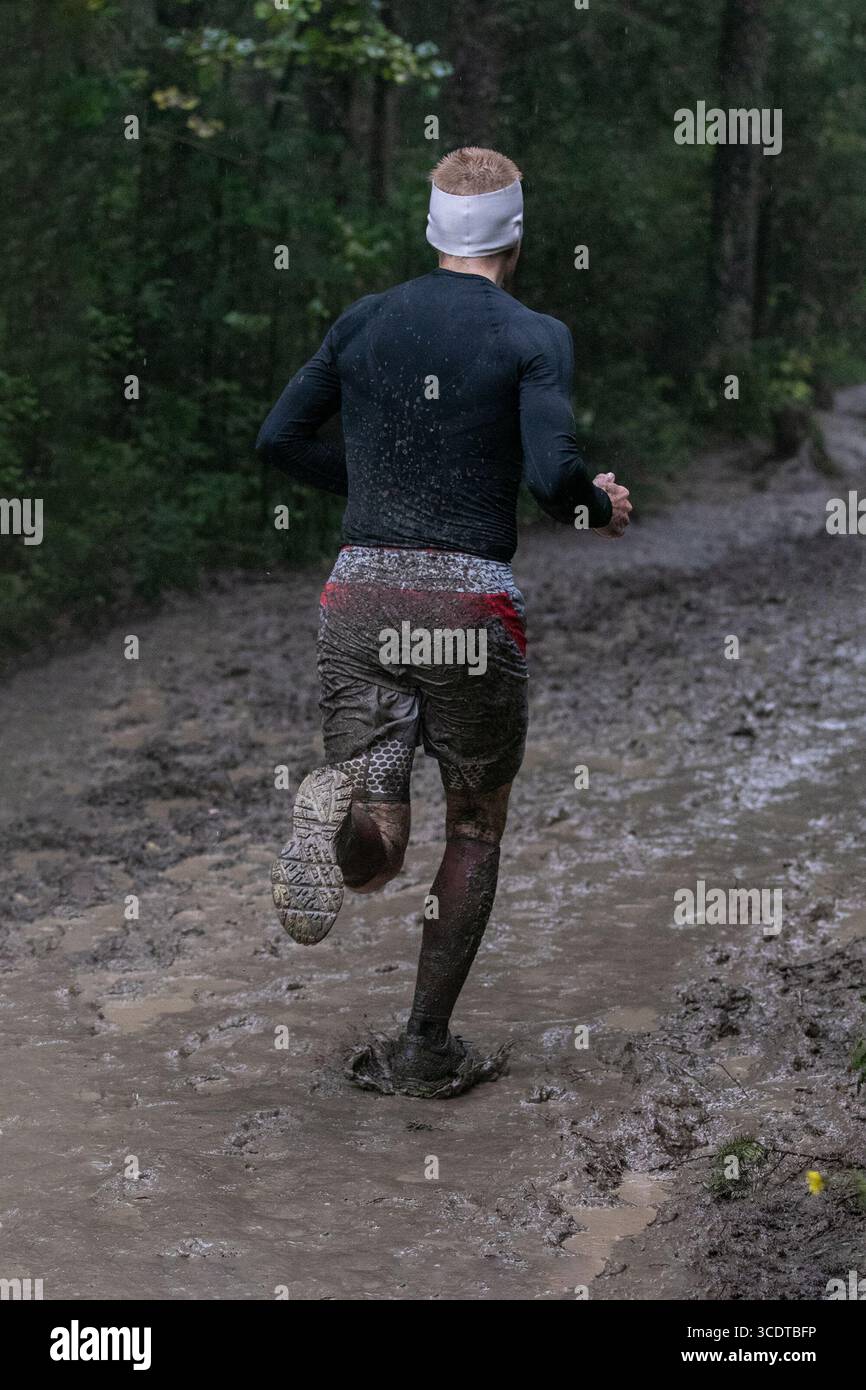 Athlete running puddles of mud in heavy rain during forest marathon ...