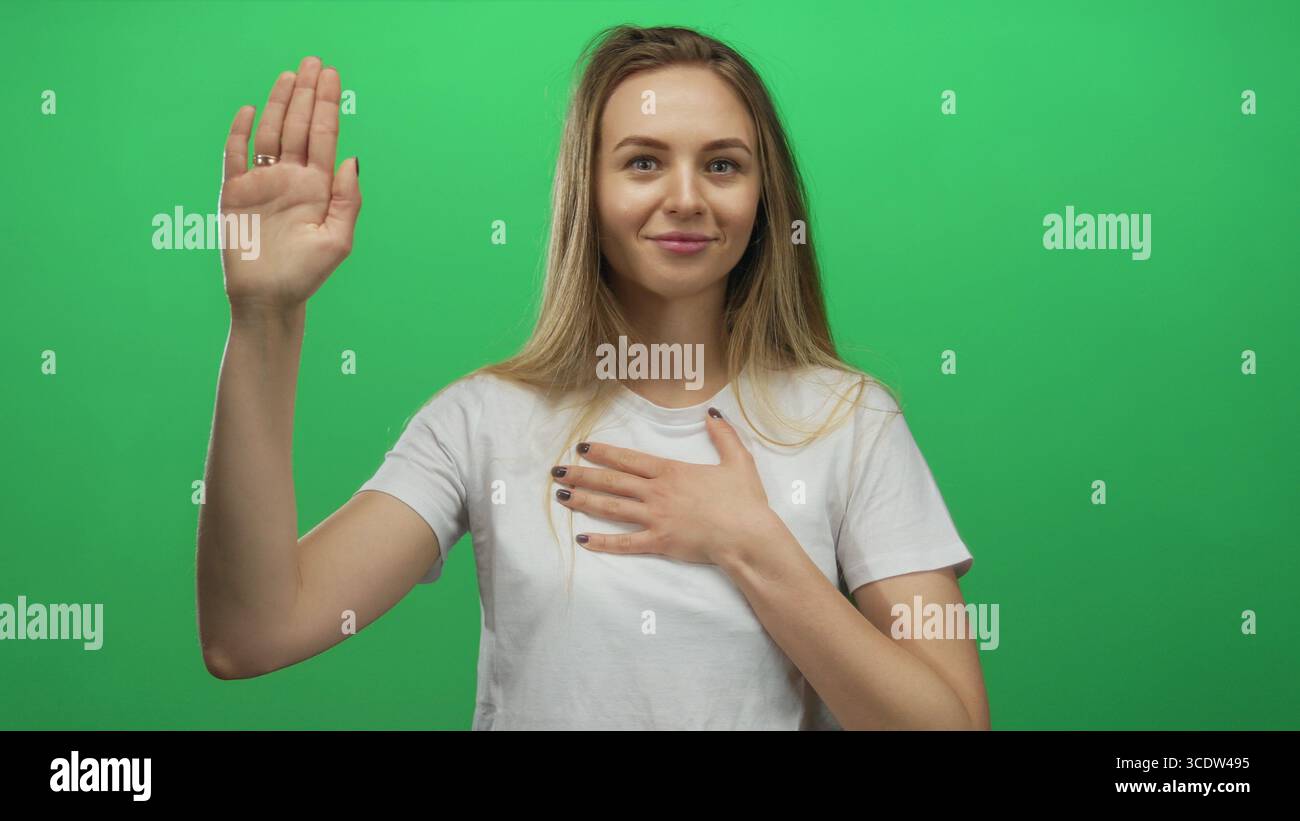 Woman raising hand in a pledge gesture standing against a green ...