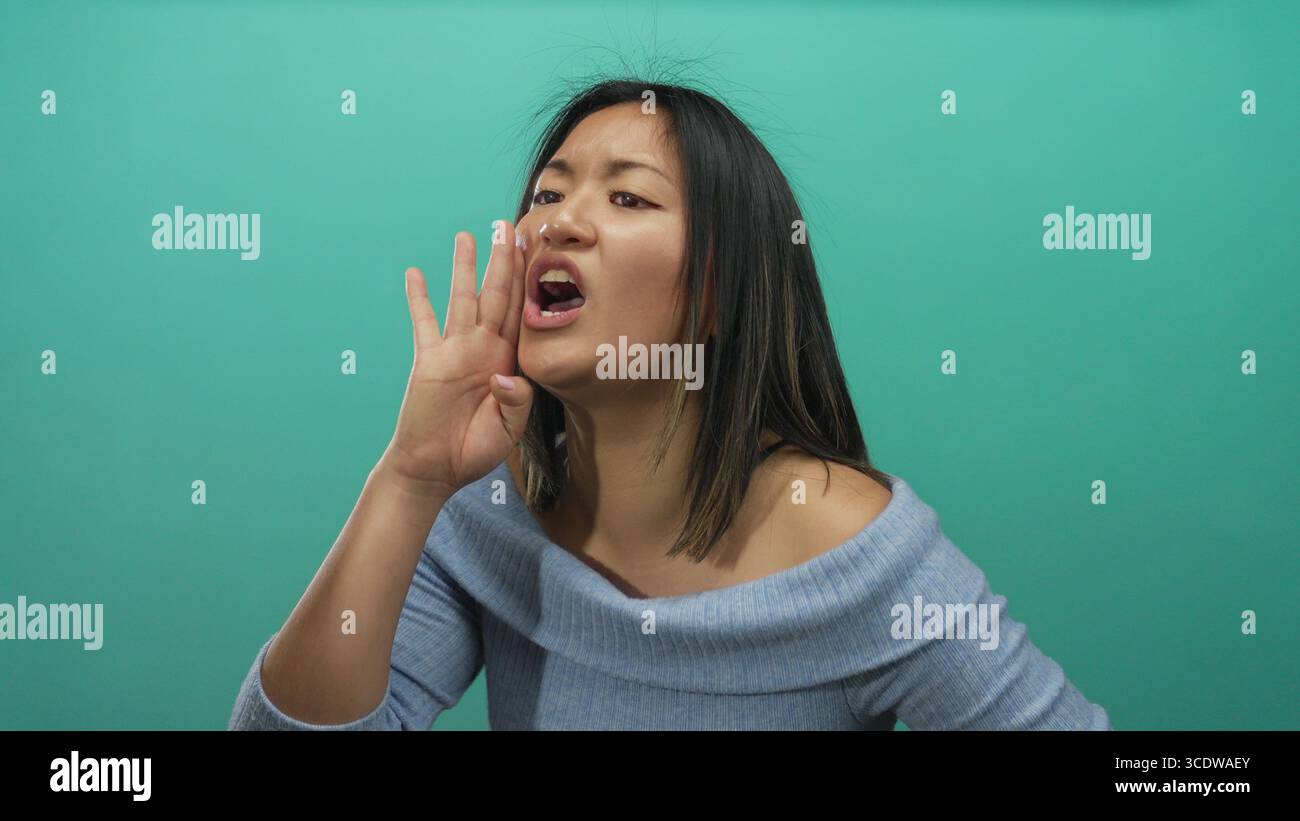 Woman shouting over isolated green background in casual attire ...