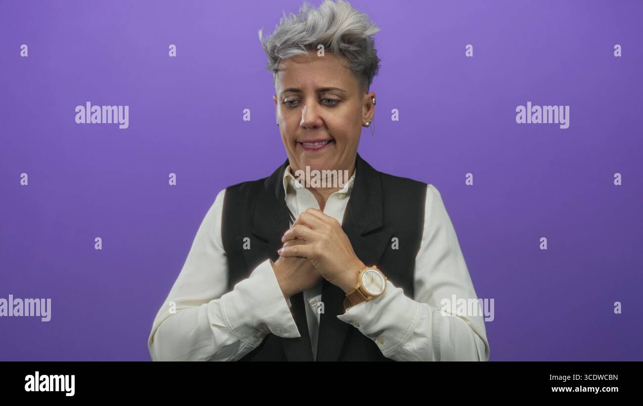 Woman with short silver hair clasping hands over chest in purple studio ...