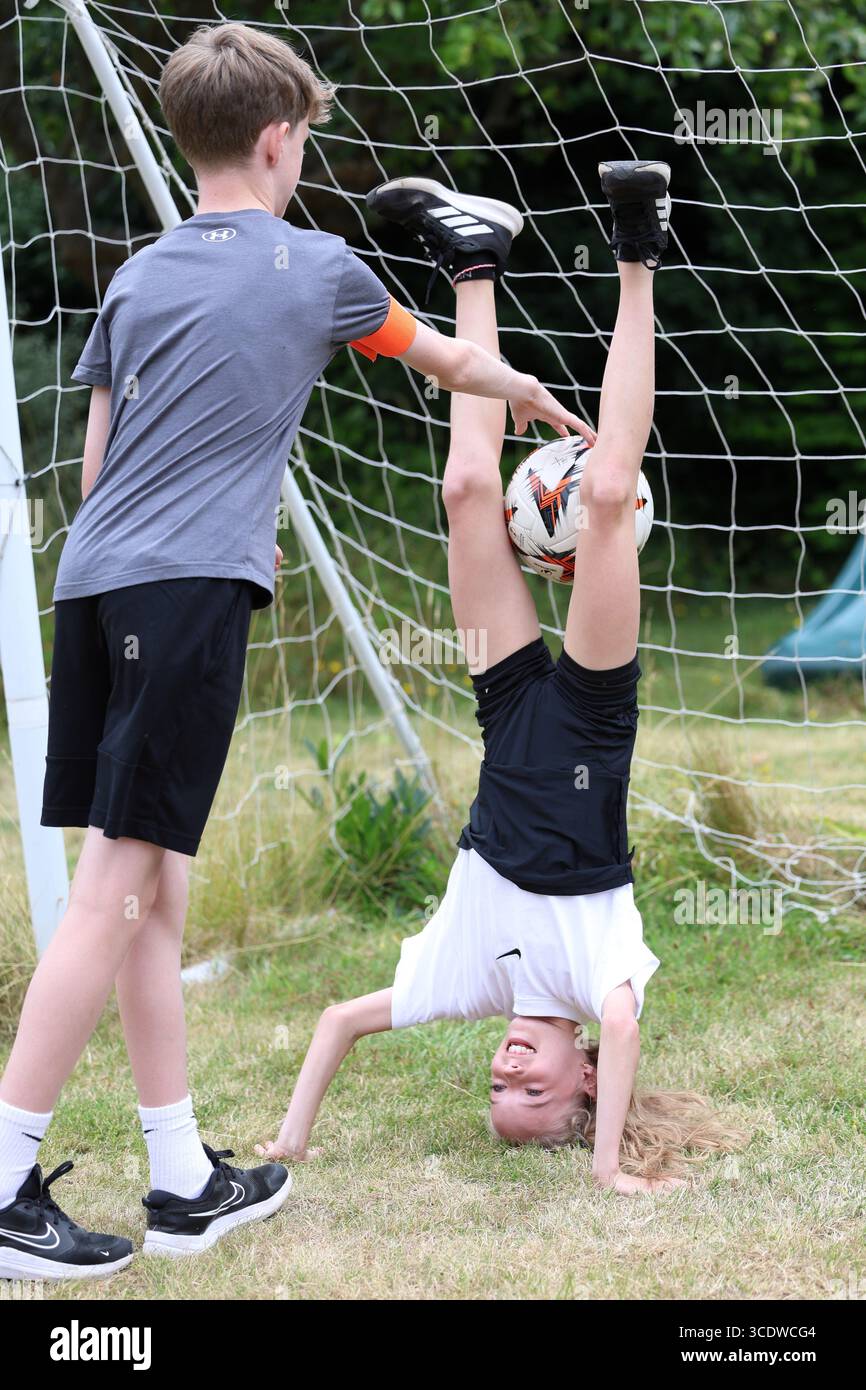 Boy helps girl upside down doing headstand hold football between legs ...