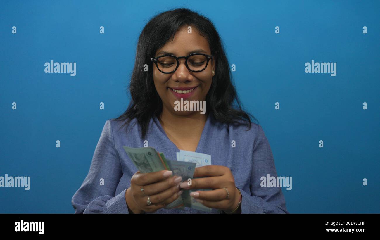 Woman counting malaysian ringgit banknotes in blue studio with glasses ...