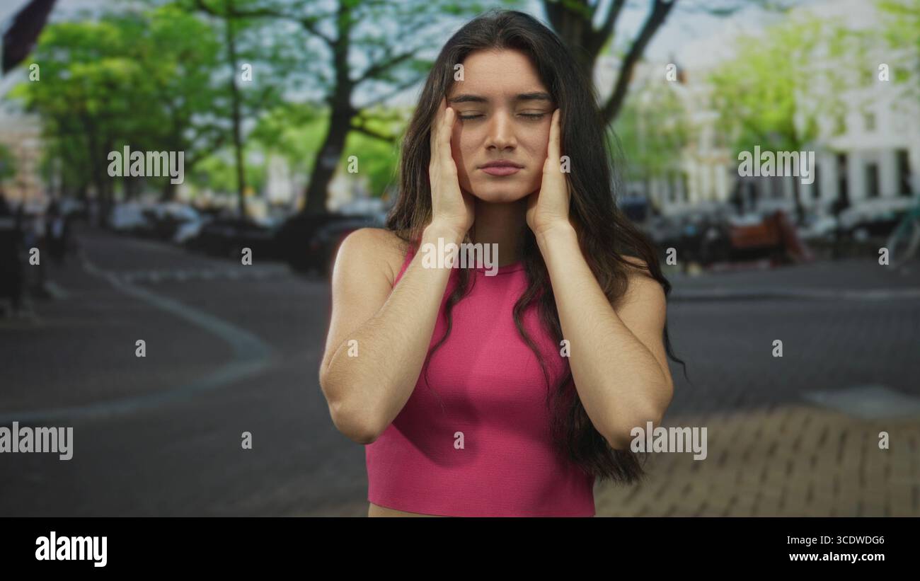 Young woman presses temples on street with pained expression and ...