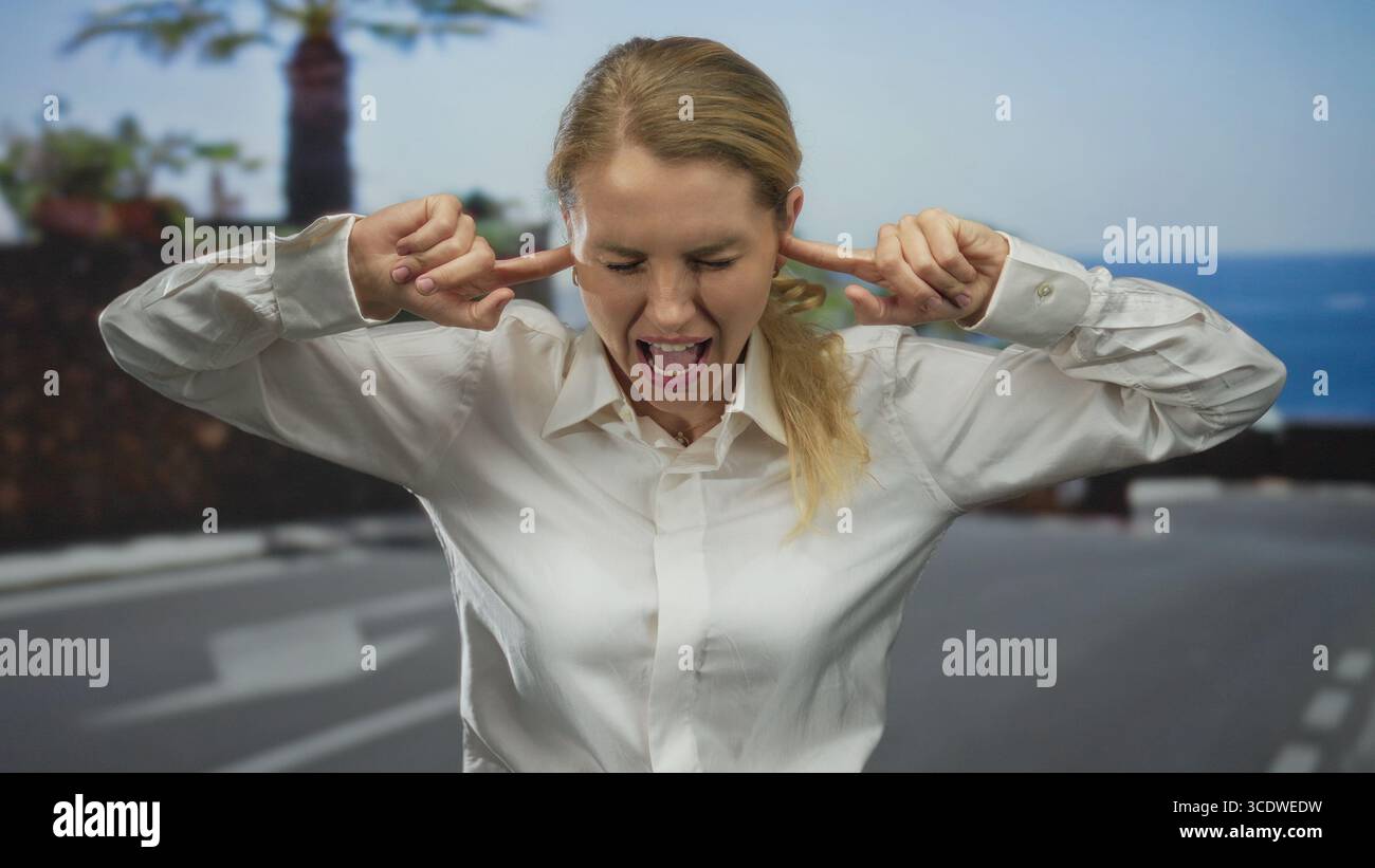 Woman plugging her ears in frustration on a city street, expressing ...