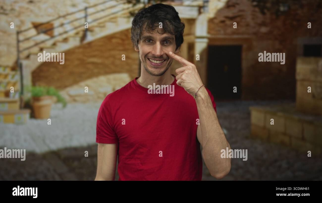 Man in red shirt pointing finger to cheek on sunlit historic old town ...